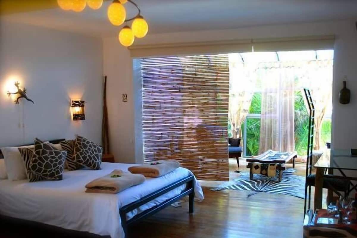 Quarto com cama, tapete estampado com padrão de zebra, pequena mesa e vista para o verde lá fora.