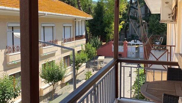 Uma varanda com vista para uma área residencial, incluindo um edifício com telhado de azulejos e entrada com portão.