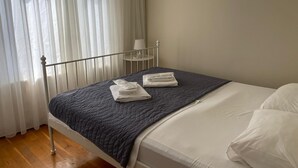 Uma cama bem arrumada com colcha escura, almofadas brancas e toalhas dobradas.