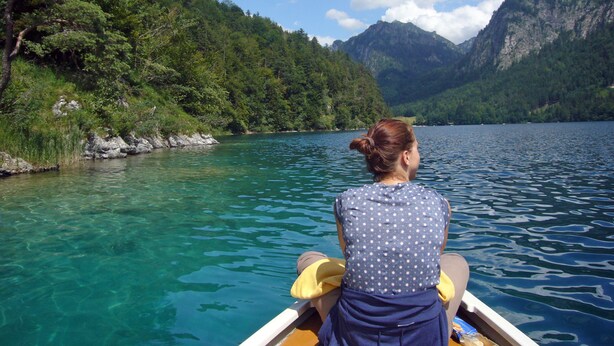 Uma mulher num barco em um lago calmo, com montanhas ao fundo.