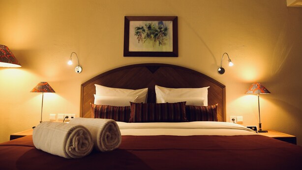 Quarto de hotel com uma cama bem arrumada, duas luminárias de cabeceira e uma obra de arte emoldurada na parede.