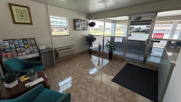 Uma área de recepção com balcão, cadeiras, um quadro emoldurado, televisão e vista para o exterior.