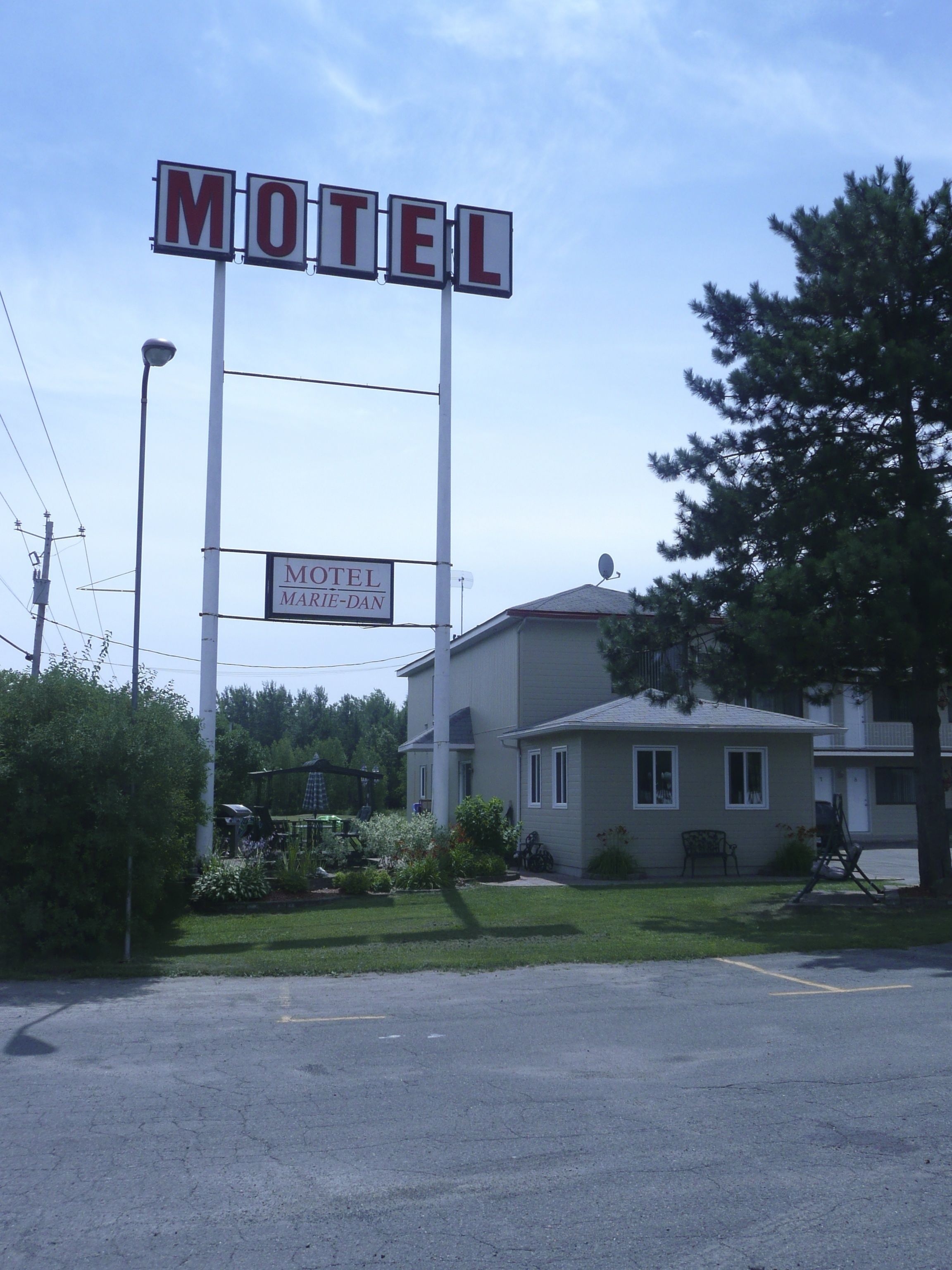 Placa de motel com o nome 'Motel Marie-Dan' e um edifício com estrutura de um andar e telhado inclinado.