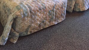 Quarto com duas camas, cada uma com colcha estampada, mesa de cabeceira com telefone e livros, e luminária fixada na parede.