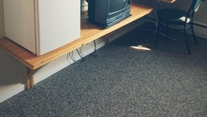 Um quarto pequeno com um frigorífico branco, uma televisão sobre uma mesa de madeira e uma cadeira.