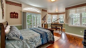 Quarto com uma cama, um piano e uma janela grande.