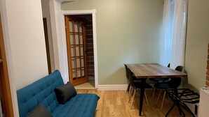 Quarto com sofá azul, mesa de jantar de madeira com cadeiras e piso de madeira.