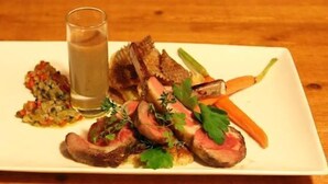 Um prato com carne fatiada, legumes e um copo de bebida sobre uma mesa de madeira.