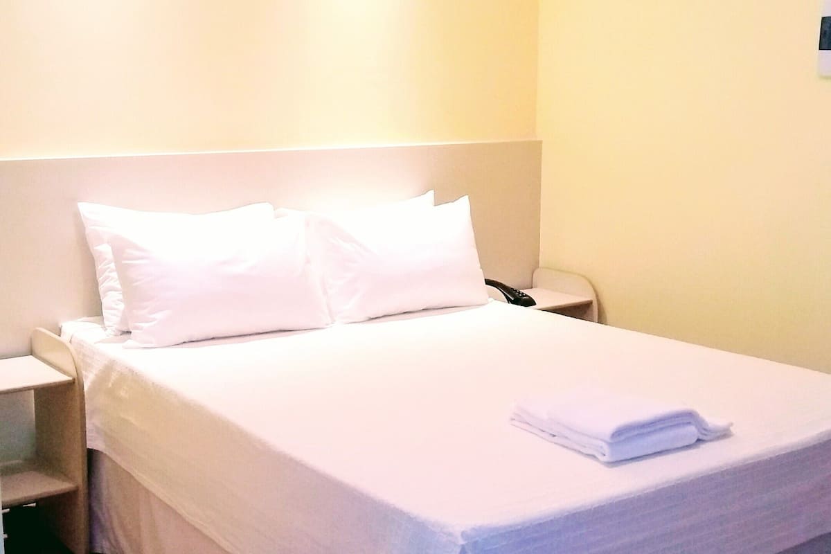 Cama bem arrumada com lençóis brancos em quarto de hotel.