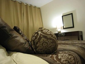 Quarto de hotel com cama, mesa de cabeceira, abajur e espelho na parede.