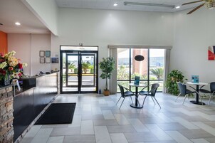 Uma área de recepção com balcão, uma janela grande e um espaço de estar com cadeiras e uma mesa.