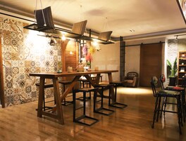 Uma sala de jantar com mesa e cadeiras de madeira, azulejos decorados nas paredes e luminárias pendentes.