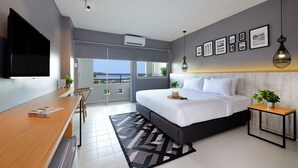 Quarto moderno com cama, escrivaninha, TV e varanda com vista.