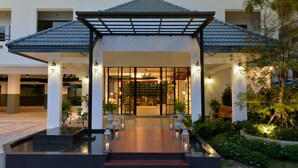 Entrada moderna de hotel com um alpendre coberto, portas de vidro e área de estar externa.