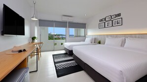 Quarto de hotel moderno com uma cama grande, uma escrivaninha com uma TV e vista da cidade por grandes janelas.