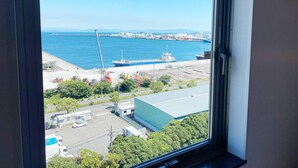 Vista da janela sobre um porto com uma guindaste, um navio grande e edifícios industriais.