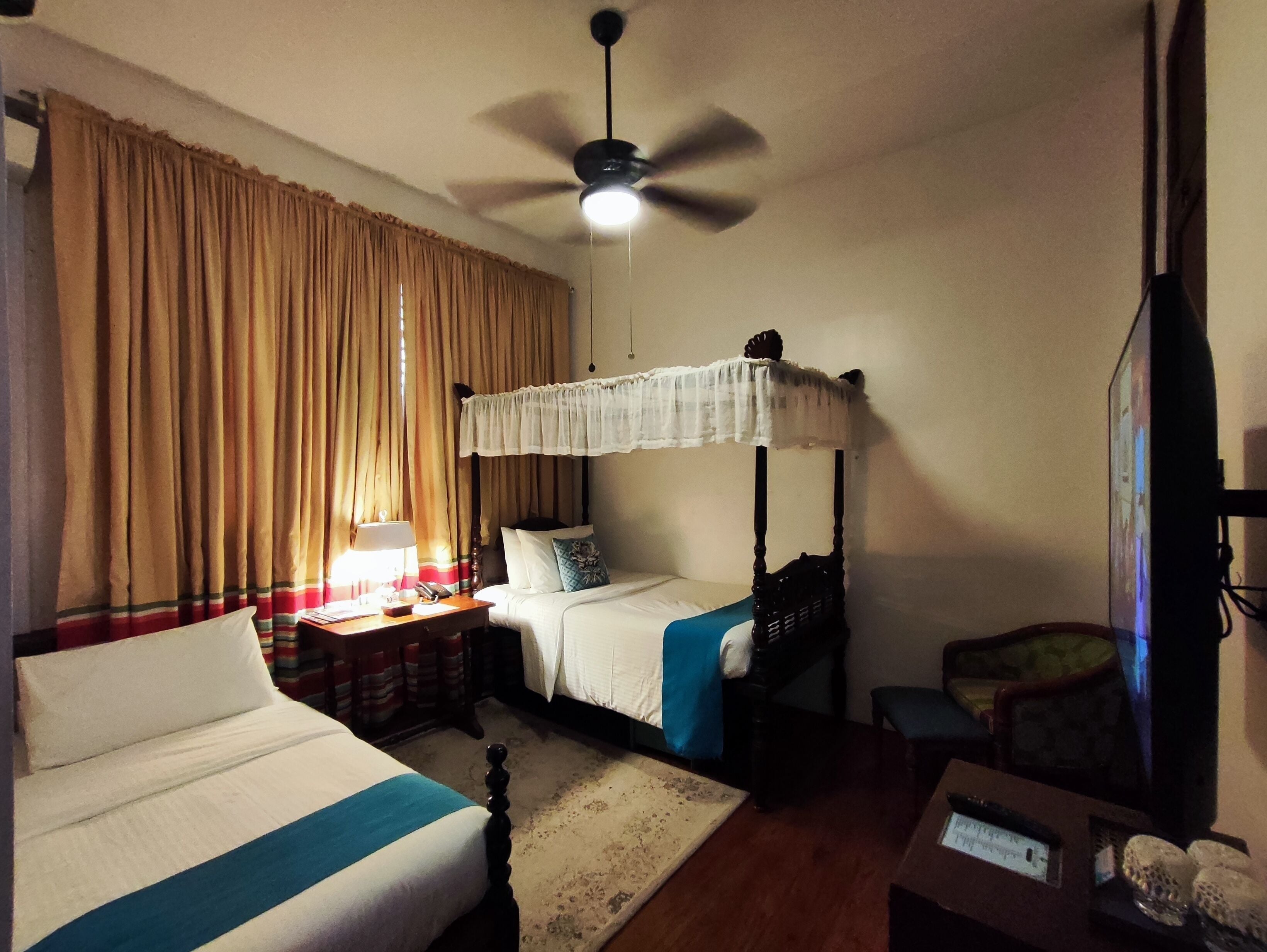 Quarto de hotel com cama beliche, escrivaninha com luminária, cadeira e televisão.