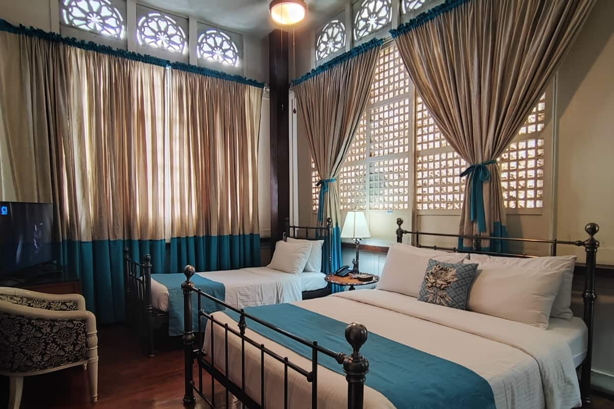 Quarto com duas camas, piso de madeira, ventilador de teto e televisão.