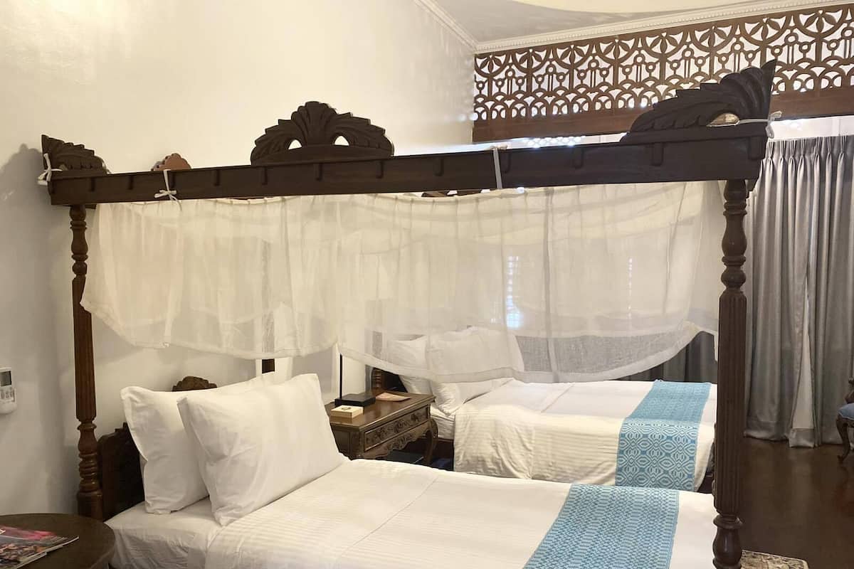 Uma cama de dossel com cortina, duas mesas de cabeceira e um painel decorativo na parede.