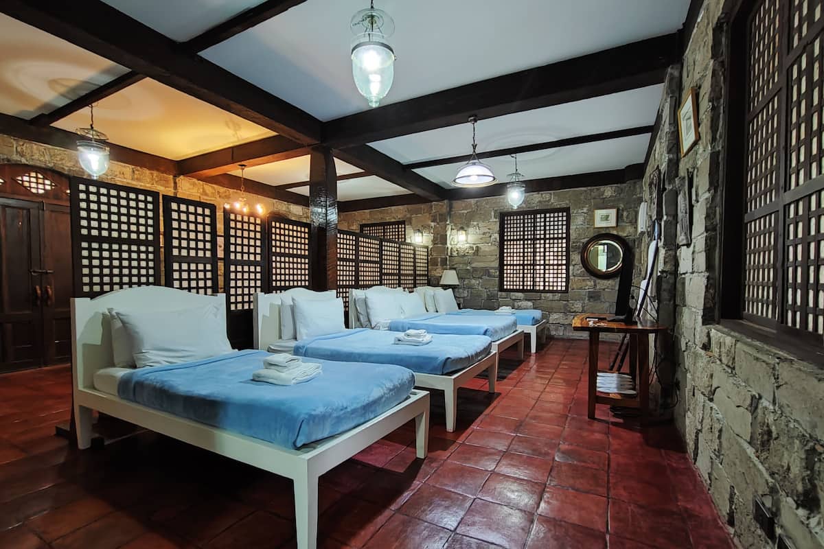 Quarto com duas camas, vigas de madeira, paredes de pedra e piso de azulejos.