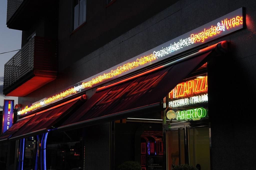 Um edifício com um letreiro de neon que diz 'Pizza' e 'Aberto', indicando que o estabelecimento está aberto.