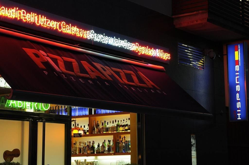 Um restaurante com um letreiro de neon que diz 'PIZZA' e um espaço de bar com prateleiras de garrafas.