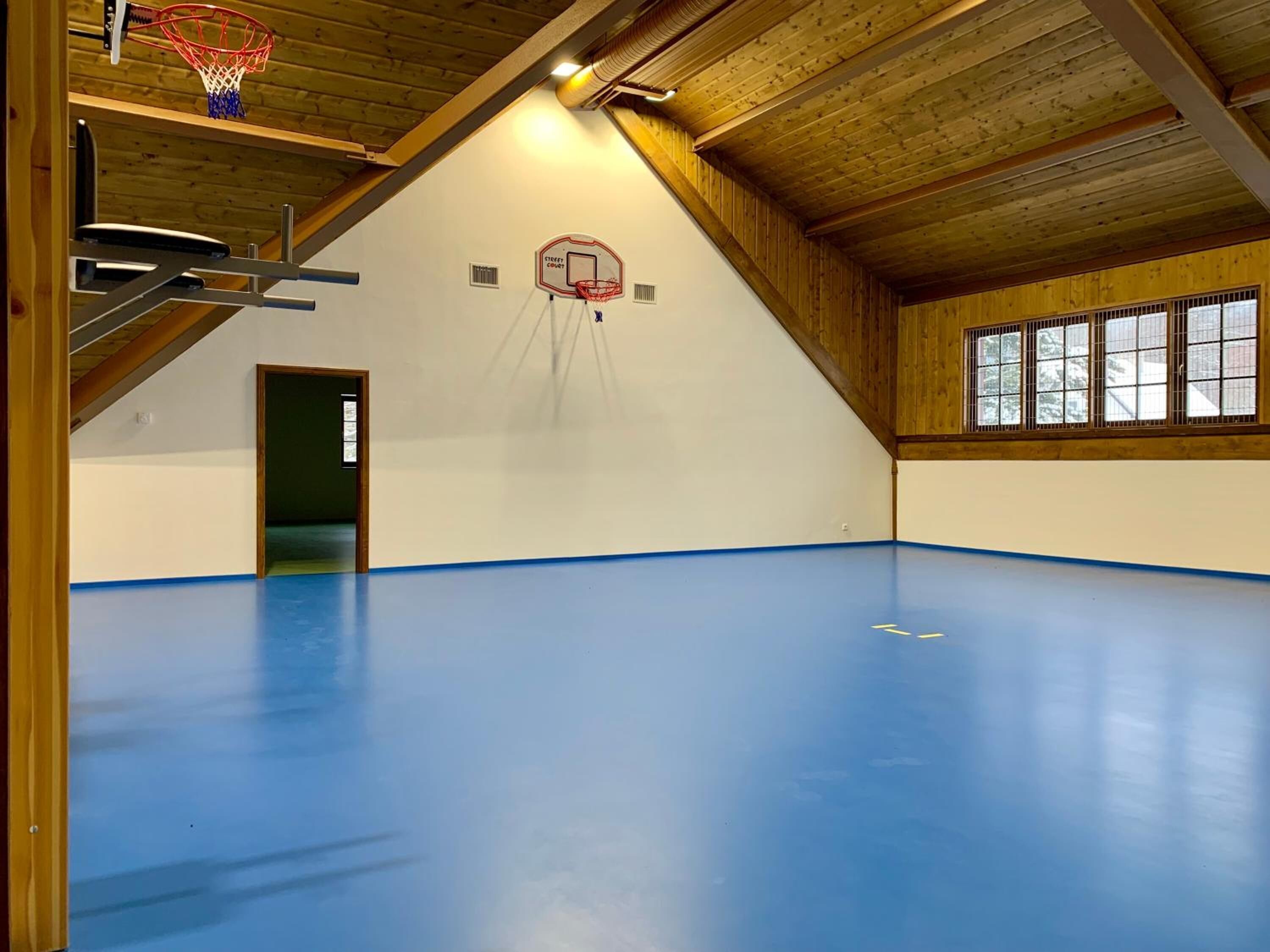 Quadra de basquete interna com teto de madeira e cesta.