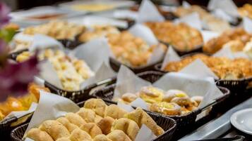 Buffet com diversos produtos de panificação, incluindo pães e doces, dispostos em bandejas.