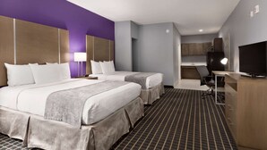 Quarto de hotel com duas camas, uma escrivaninha, uma cadeira, televisão e cozinha compacta.