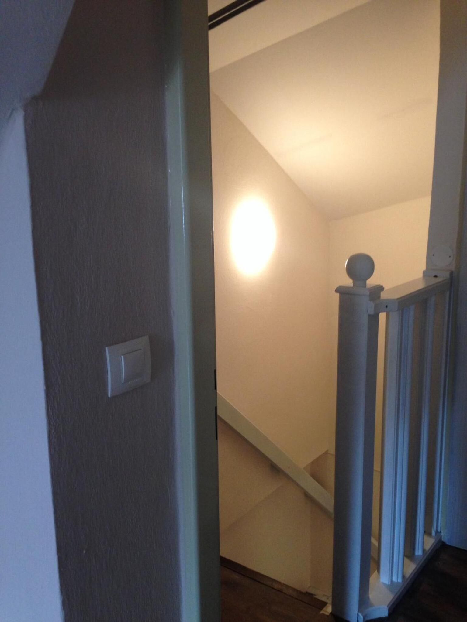 Uma escadaria com corrimão branco e um aparelho de iluminação no topo.