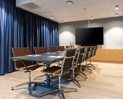 Uma sala de conferência com uma mesa comprida, várias cadeiras, uma televisão de tela plana grande e um fundo de cortina azul.