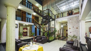 Um hall amplo com uma mesa amarela, assentos de couro, escada e plantas em vasos.
