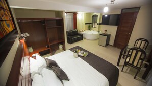 Quarto de hotel com cama, escrivaninha, cadeira, pequeno sofá, banheiro com banheira e guarda-roupa.