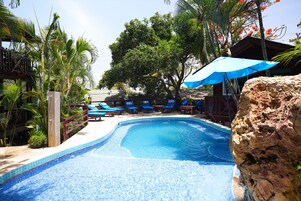Uma piscina cercada por vegetação tropical, com espreguiçadeiras e guarda-sóis.