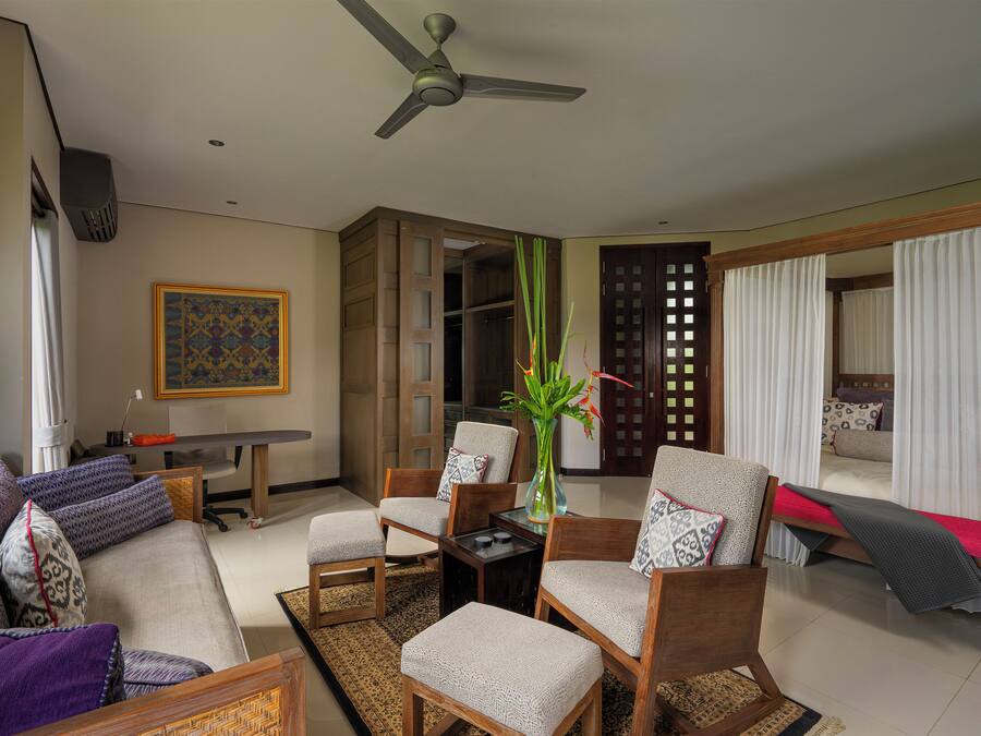 Sala de estar com sofá, cadeiras, mesa de centro, ventilador de teto, pintura e cama com cortinas.