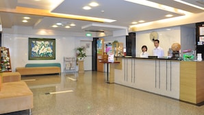 Uma área de recepção de hotel com balcão, relógio, planta e um espaço de estar com um banco.