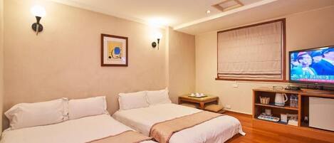 Quarto de hotel com duas camas, televisão, uma mesa pequena com abajur e janela com persianas.