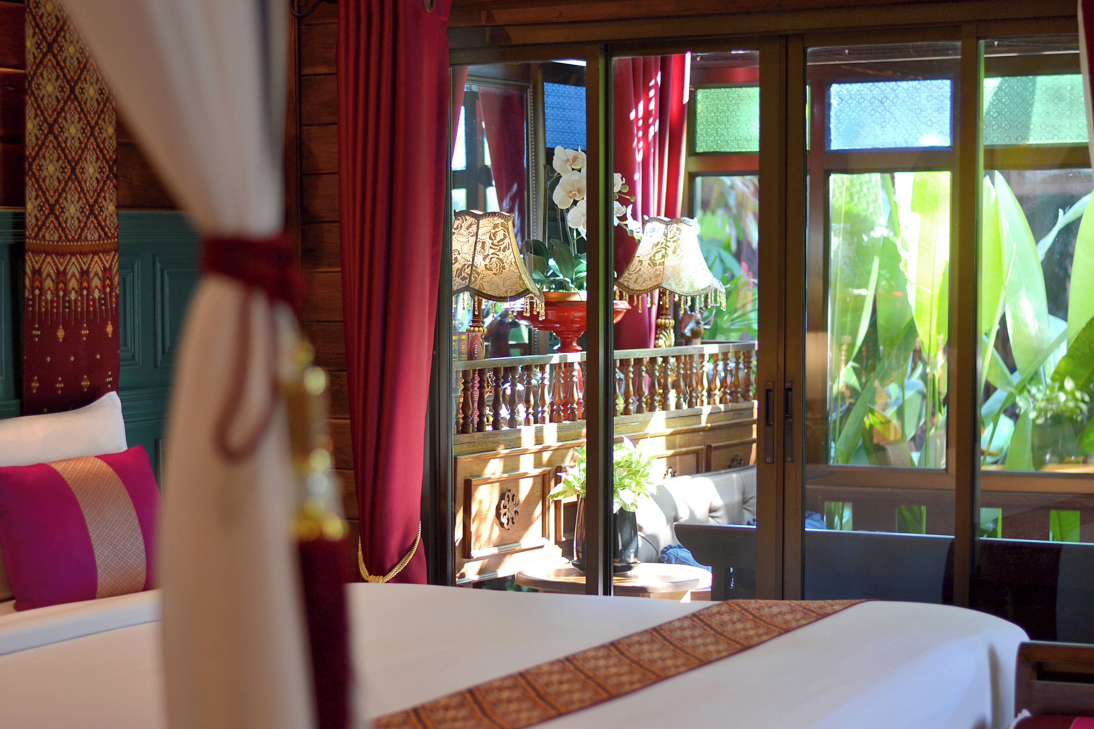 Quarto de hotel com cama, cortinas, janela com vista para vegetação e varanda com guarda-corpo.