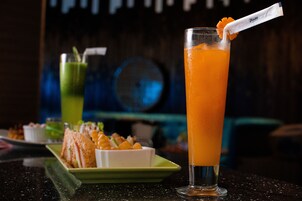 Um copo alto de suco de laranja com canudo e um enfeite de flor sobre um balcão de bar.