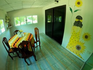 Uma área de refeições com mesa redonda, cadeiras e um mural na parede.