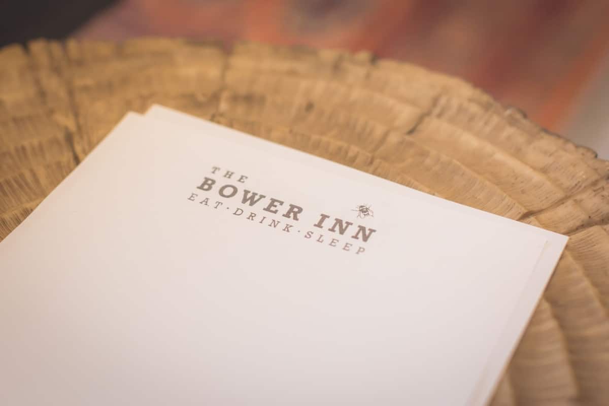 Um menu ou cartão informativo com o título "The Bower Inn" e o subtítulo "Comer, Beber, Dormir".