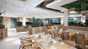 Um restaurante moderno com mobiliário de madeira, um balcão central e plantas em vasos.