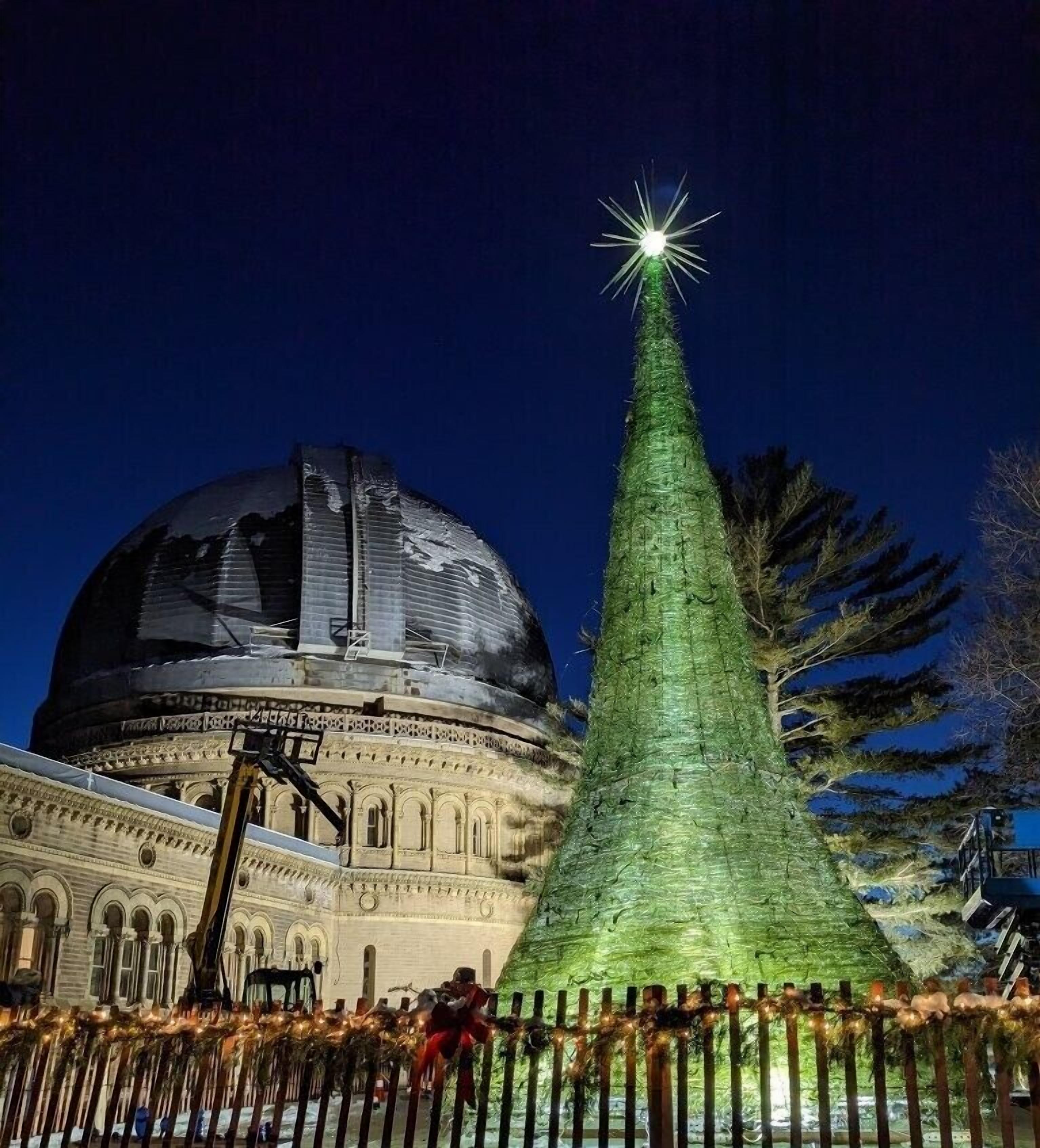Uma grande estrutura em forma de cúpula com um objeto verde em formato de cone na frente, possivelmente uma escultura, e uma luz semelhante a uma estrela no topo.