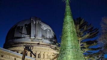 Uma grande estrutura em forma de cúpula com um objeto verde em formato de cone na frente, possivelmente uma escultura, e uma luz semelhante a uma estrela no topo.