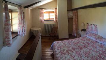 Quarto com cama de madeira, uma mesa redonda, uma cadeira e janela com cortinas.