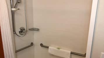 Duche amplo com barra de apoio e chuveiro manual na parede.