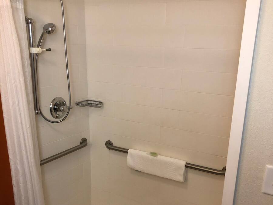Duche amplo com barra de apoio e chuveiro manual na parede.