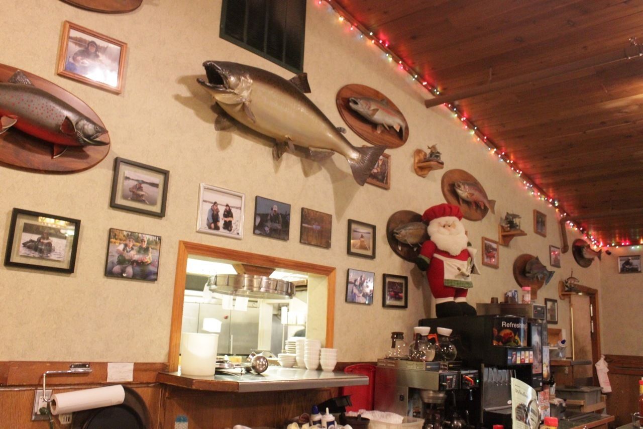 Interior de restaurante com peixes montados na parede, área de cozinha e decoração natalina.