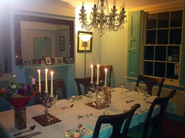 Uma sala de jantar com mesa posta para quatro pessoas, velas, um candelabro e um espelho.