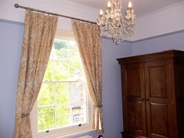 Um quarto com uma grande janela, cortinas, um candelabro e um armário de madeira.
